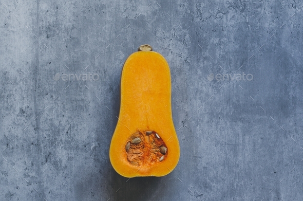 Winter butternut squash gourd sliced in half on a grey background with ...