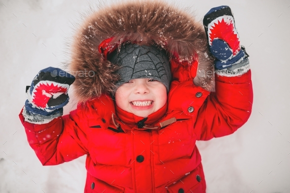 Portrait of a happy cute boy in red winter jacket playing with snow in ...