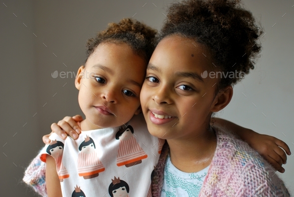 Portrait of a two sibling girls of mixed race (sisters) wearing a knit ...