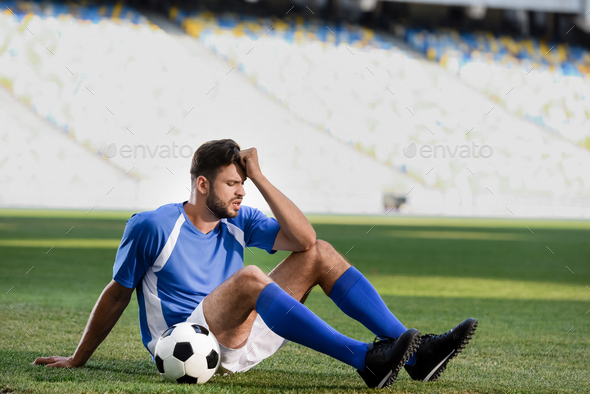 sad professional soccer player in blue and white uniform sitting with ...