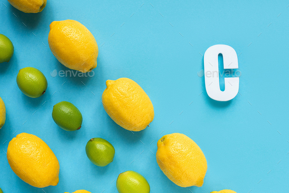flat lay with ripe yellow lemons, green limes and letter C on blue ...