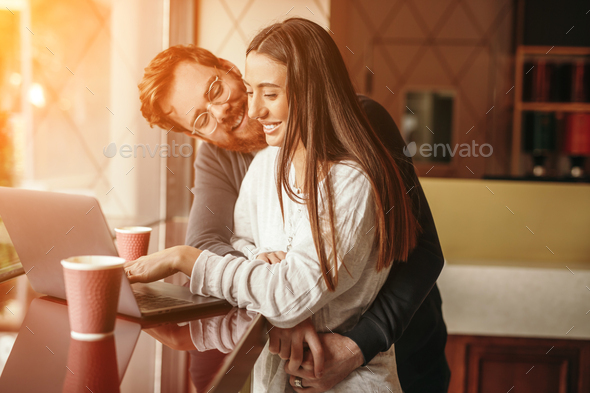 Smiling man hugging woman working on laptop at table Stock Photo by kegfire