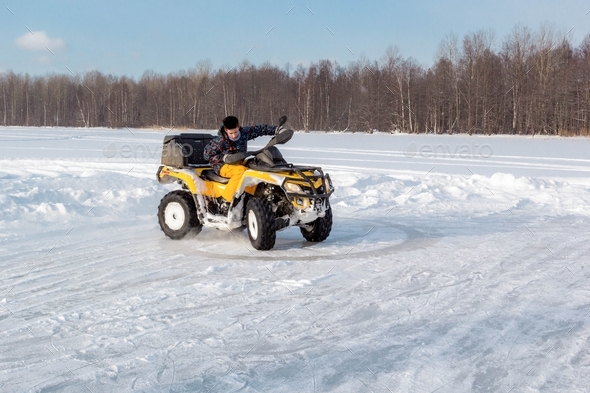 Young man rides ATV on ice on snow frozen lake in cold sunny winter day ...