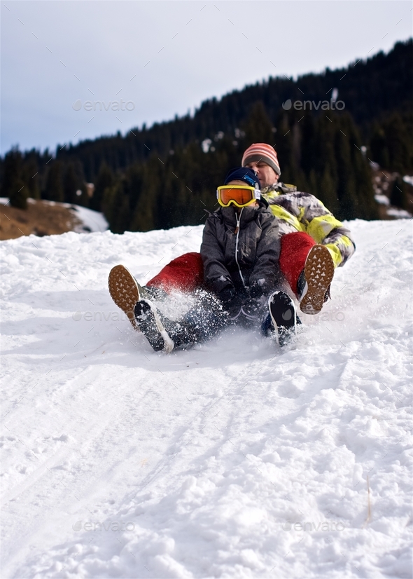 Young man and little boy have fun on sleds and descend from the snow ...
