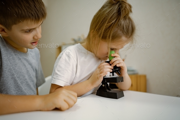 Children, girl and boy at home in the room look through microscope ...