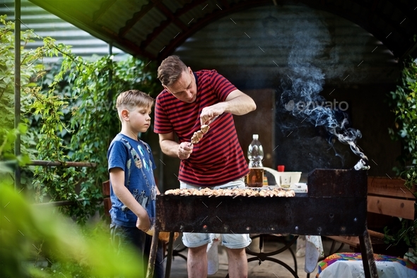 Young man and little boy cooking with skewers of Kebabs meat grill with ...
