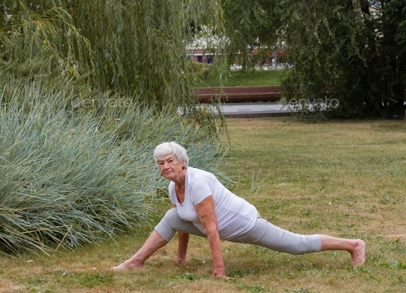 An elderly, positive, sportive woman does the splits in a summer park ...