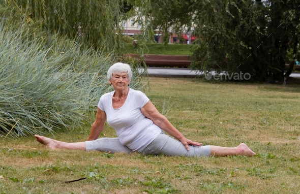 An elderly, positive, sportive woman does the splits in a summer park ...
