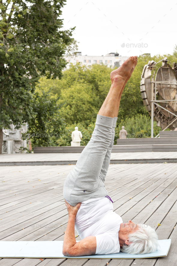 An elderly athletic woman does a candlestick exercise on a wooden ...