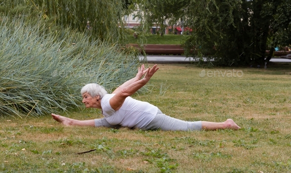 An elderly, positive, sportive woman does the splits in a summer park ...