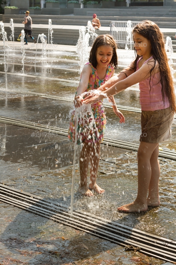 Two girls, sisters play with water jets in the fountain. Stock Photo by 12311840303