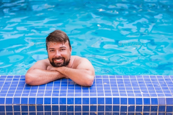 Handsome smiling man with white teeth in swimming pool in summer ...