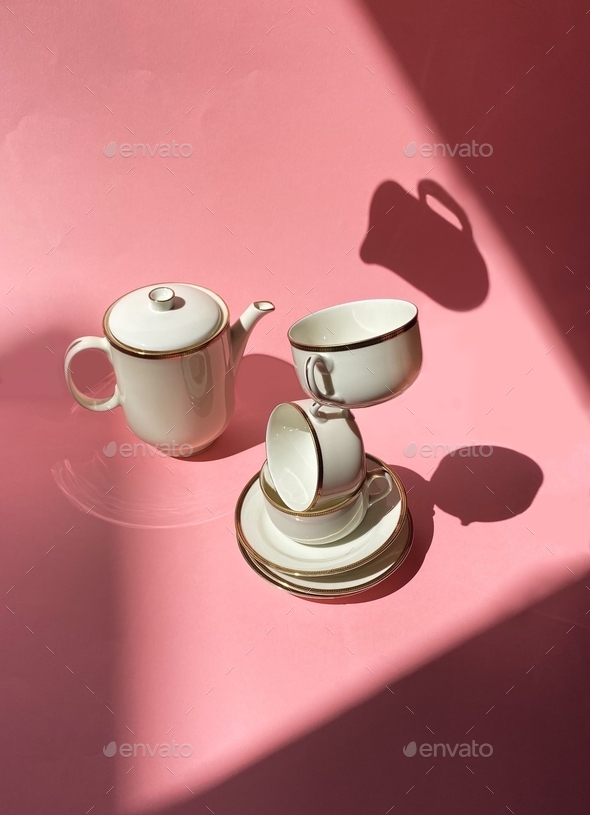 Tea set with shadow of milk jug in levitation on the pink surface. Game ...
