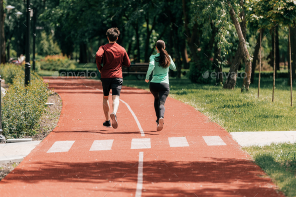 Back view of young couple jogging together on running track in park ...