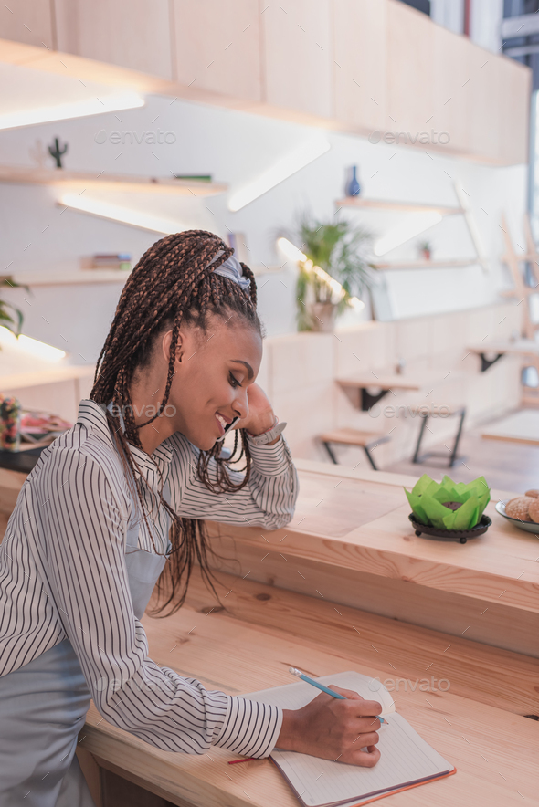 Smiling african american barista standing behind the counter and ...