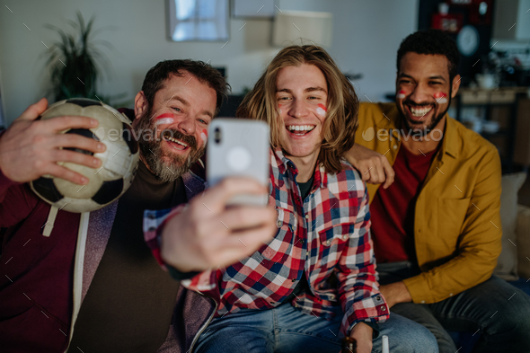 Happy football fans friends watching football at home and taking selfie ...