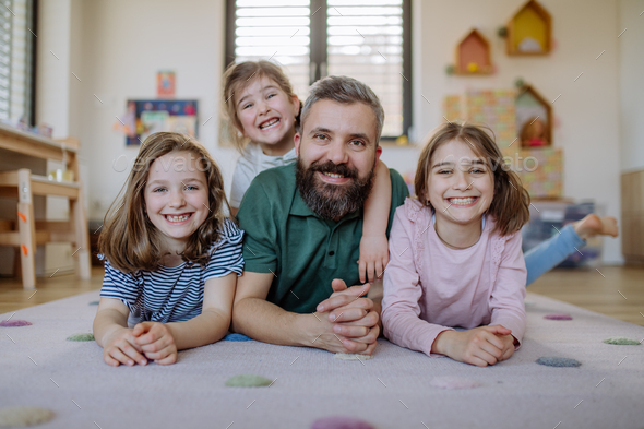 Cheerful father with three little daughters playing together at home ...