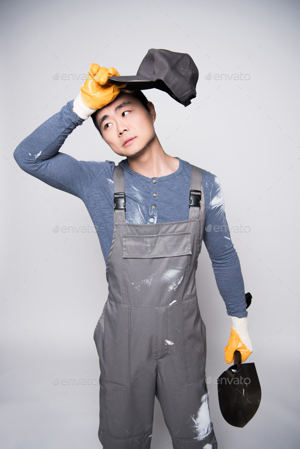 Young construction worker in overalls and safety gloves wiping the ...