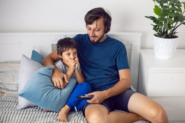 family father and son are lying on the bed with a remote control and ...
