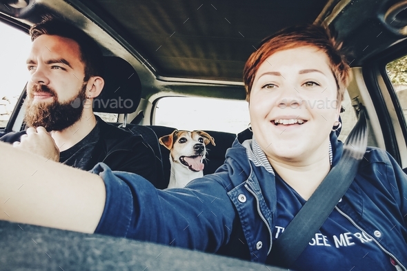 Millennial couple family with a dog riding in cars and take a selfie ...
