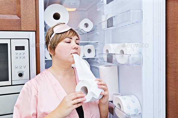 Woman in pajamas greedily eats toilet paper near the fridge filled with ...