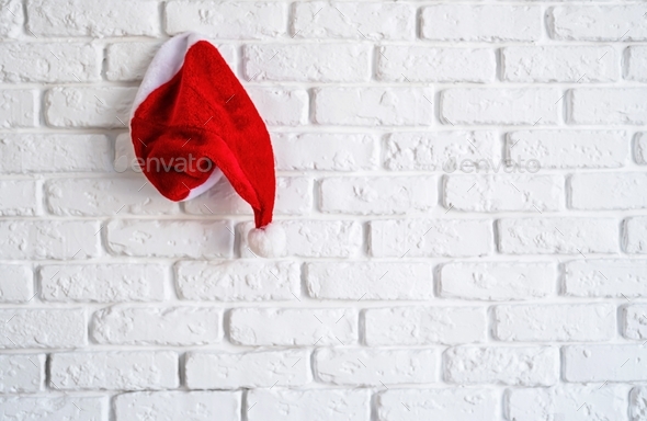 Christmas concept. Red santa hat hanging on white bricks wall with copy ...