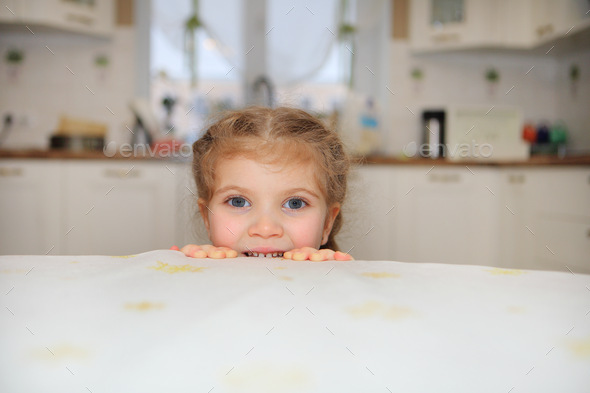 Happy child peeking from the table in the kitchen at home Stock Photo ...