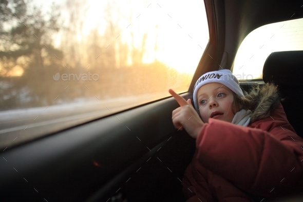 A child strapped into the car in the back seat draws on the window at ...