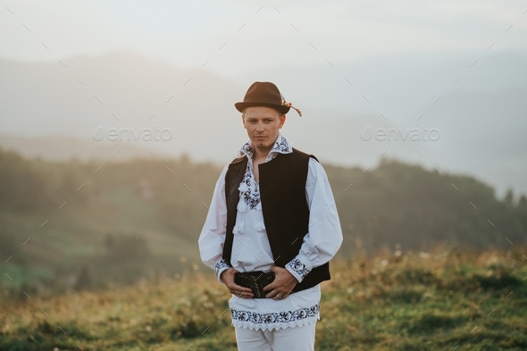 Romanian young man in traditional costume wearing a hat on a hill at ...