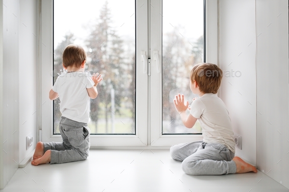 Children boys siblings look through the window on a large bright ...