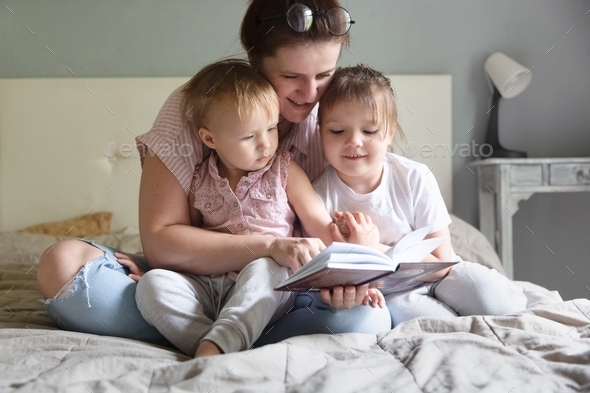 mom is reading book with two children on bed together Stock Photo by ...