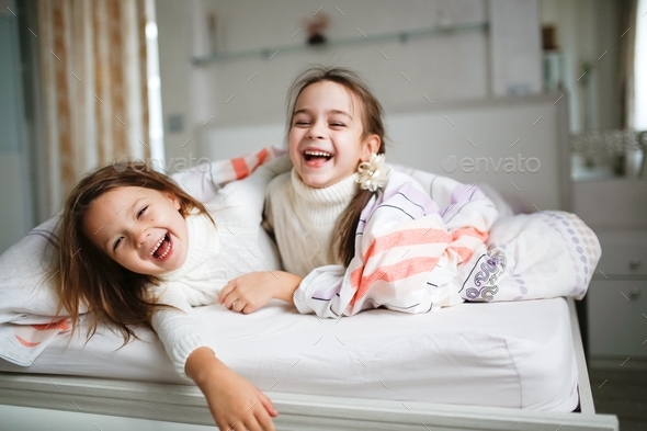 Caucasian emotional children girls friends lie on bed in the bedroom ...
