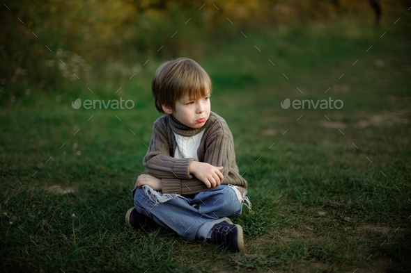 Sad boy child sits on a path in the park in the forest, a lonely child ...