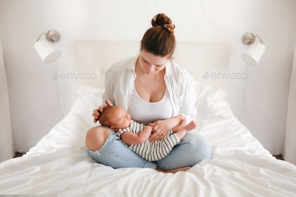 Tender Mother in white shirt holding newborn baby on bed in bedroom ...