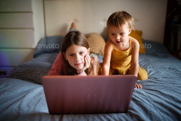 Girls children in bedroom look at laptop screen in real interior ...