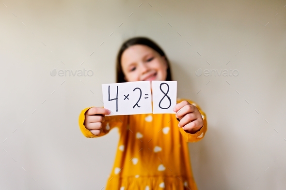cute kid girl in mustard dress learns the multiplication table on beige ...