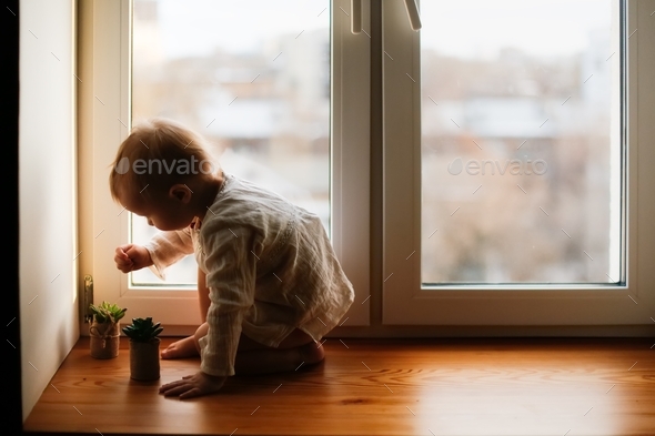 cute toddler child on the windowsill by the window playing with a ...