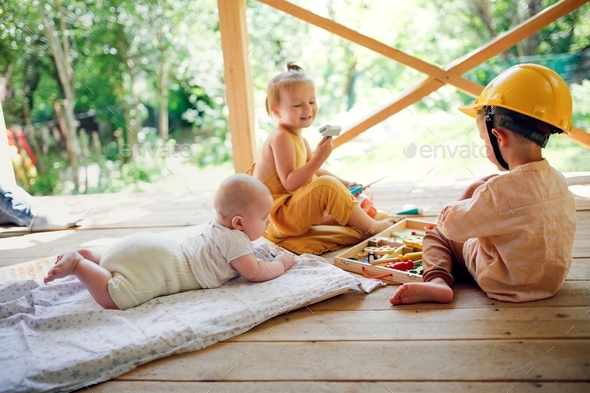 Three European sibling children play side by side on wooden porch ...