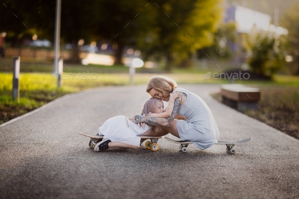 Mom and daughter sit together on skateboards. Mother hugs child girl in ...