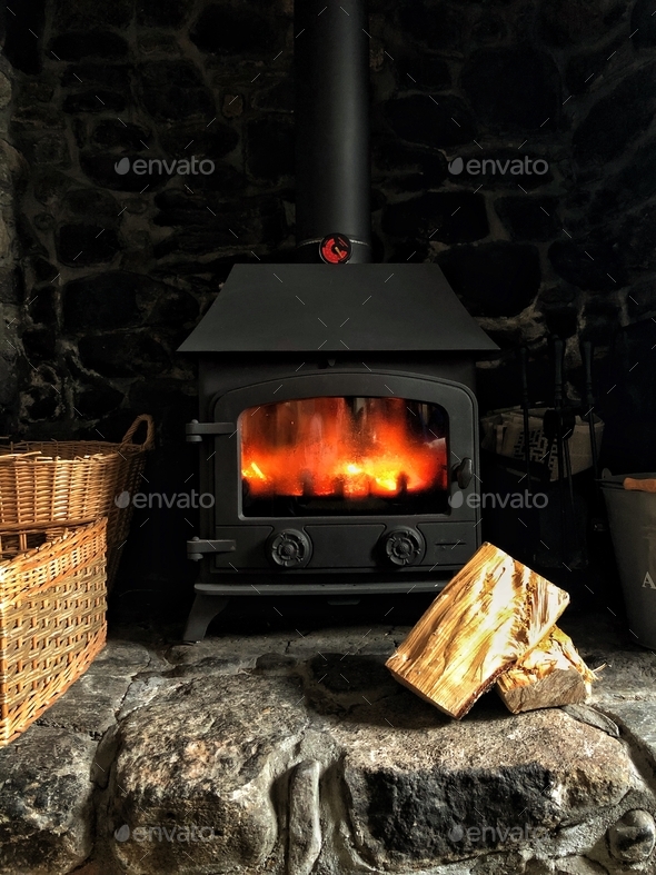 A fire ablaze in a wood burning stove keeping a cozy stone cottage warm ...