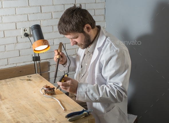 a man soldering iron solders a part from an electrical appliance. the ...