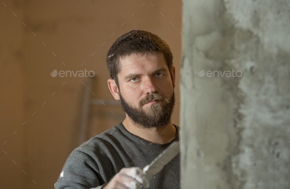 a man with a beard plasterer plasters with a spatula a concrete corner ...