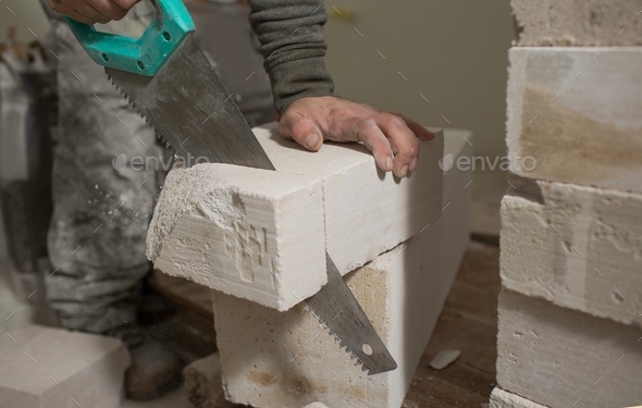 a man saws a block of foam concrete with a close-up of a hand and a ...