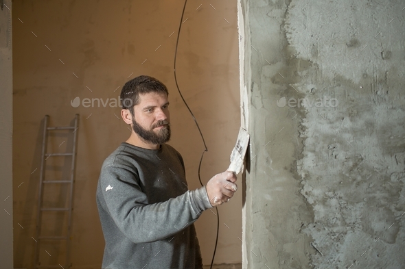a man with a beard plasterer plasters with a spatula a concrete corner ...