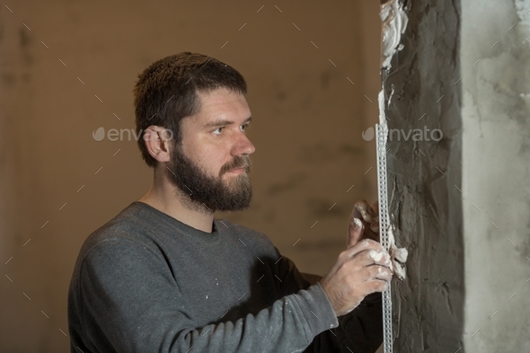 a man with a beard plasterer mounts a perforated painting corner on the ...