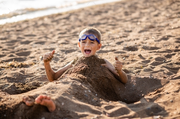 The boy lies buried in the sand and screams emotionally. Stock Photo by ...