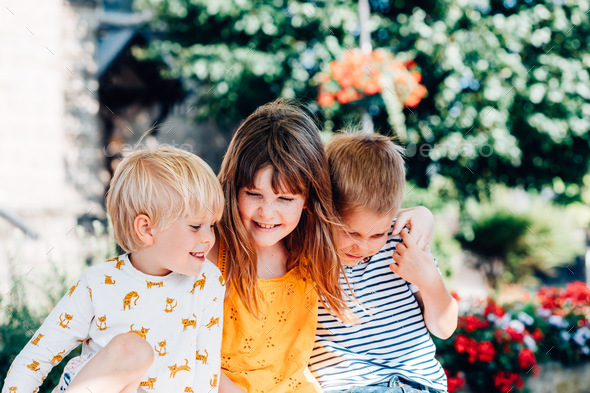 three children are sitting in an embrace, smiling, laughing, having fun ...