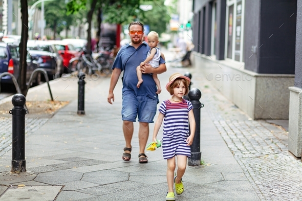 The girl is walking down the street, followed by her father with the ...