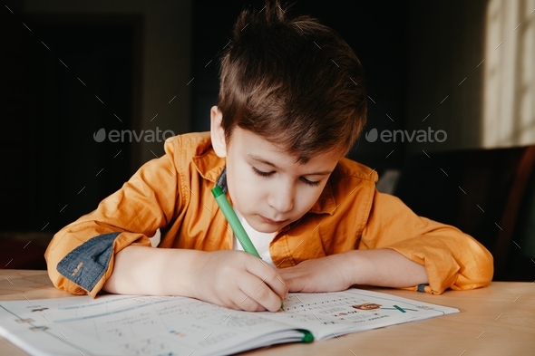 Cute 7 years old child doing his homework sitting by desk Stock Photo ...