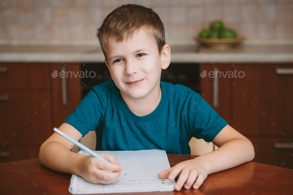 Cute child writing letters in notebook sitting by table Stock Photo by ...